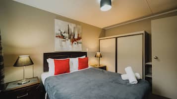 Quarto de hotel com cama, mesas de cabeceira, um quadro, guarda-roupa e uma luz no teto.