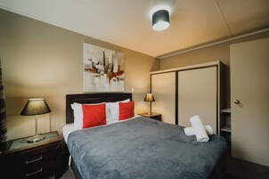 Quarto de hotel com cama, mesas de cabeceira, um quadro, guarda-roupa e uma luz no teto.