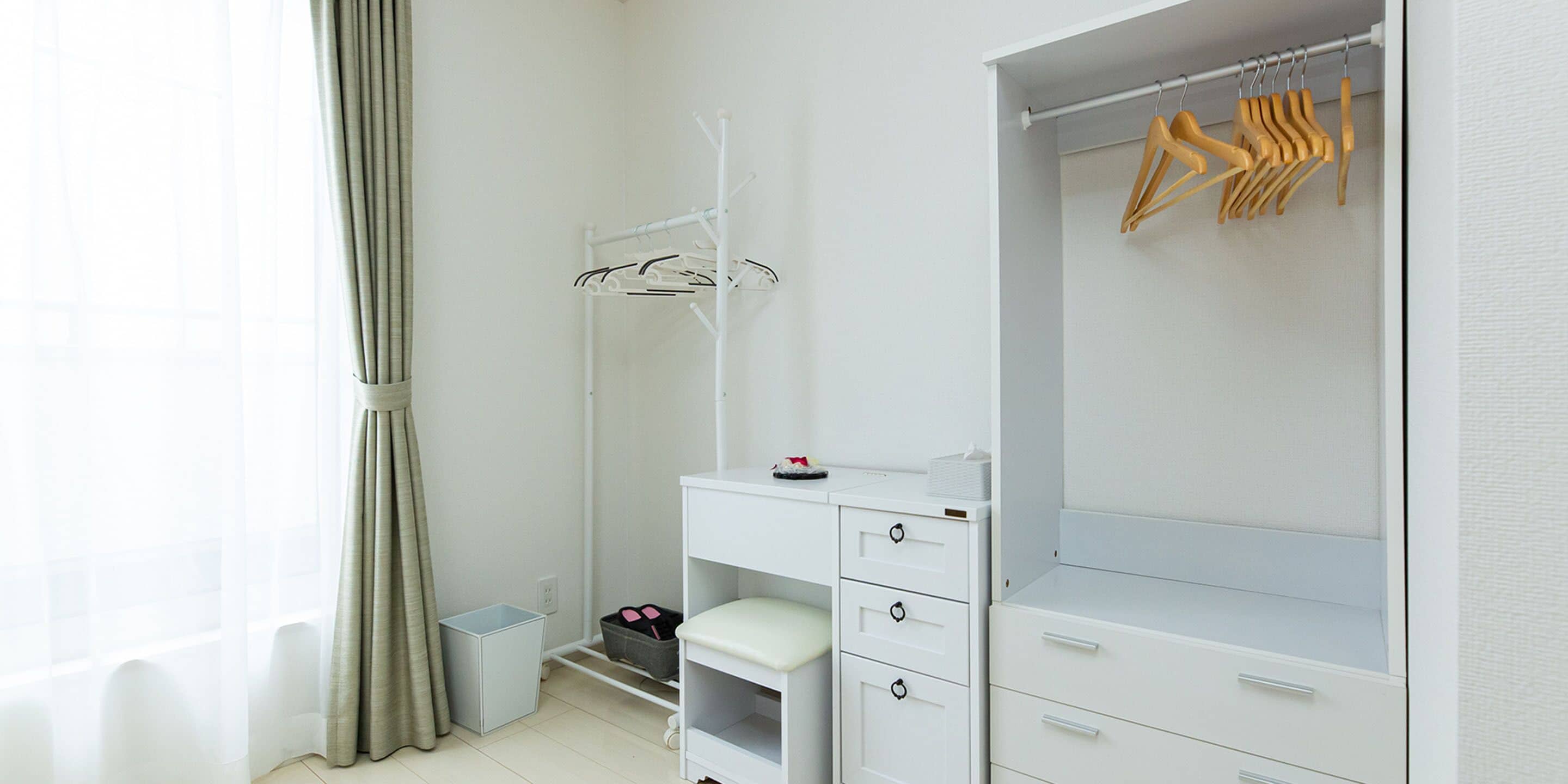 Quarto bem arrumado com um guarda-roupa branco, uma mesa de cabeceira e um cabideiro.