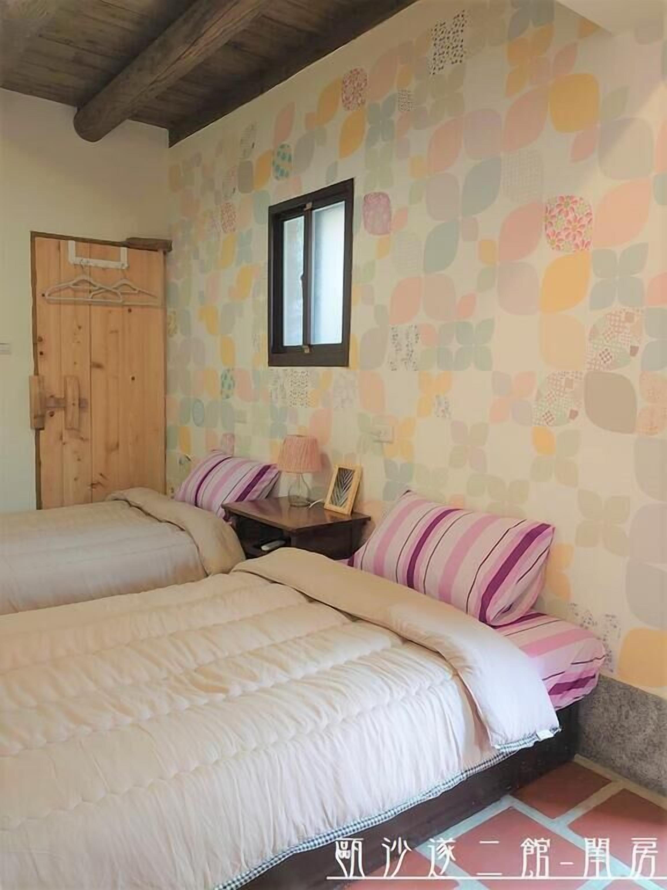 Quarto com duas camas, porta de madeira, janela e parede estampada.