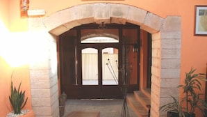Uma porta com arco de pedra que dá para um quarto com uma janela grande e uma cruz na parede.
