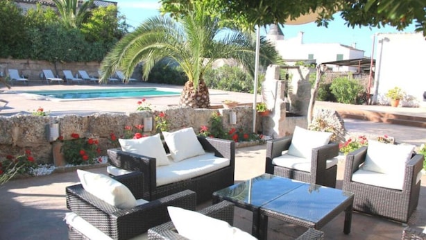 Uma área de estar externa com móveis de vime e mesa de vidro, com vista para uma piscina e vegetação exuberante.
