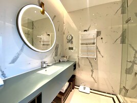 Uma casa de banho moderna com uma toucador de mármore, um espelho grande, um porta-toalhas e uma cabine de duche em vidro.