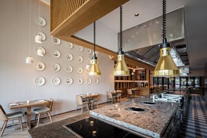 Interior moderno de restaurante com área de bar, teto de madeira e pratos fixados na parede.