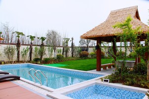 Uma piscina com cobertura de palha, rodeada por vegetação e um gramado bem cuidado.