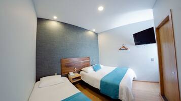 Quarto de hotel com duas camas, cabeceira de madeira, televisão fixada na parede e piso de madeira.