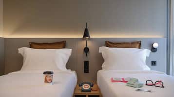 Quarto de hotel com duas camas, um abajur, um telefone, uma xícara de café e um par de óculos na cama.