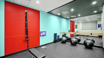 Academia com equipamentos de ginástica, um espelho e parede em vermelho e verde-água.