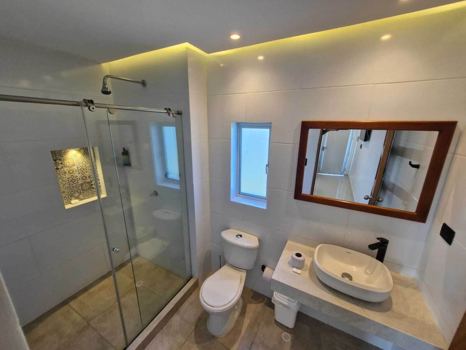Casa de banho moderna com chuveiro em cabine de vidro, sanita, lavatório e espelho.