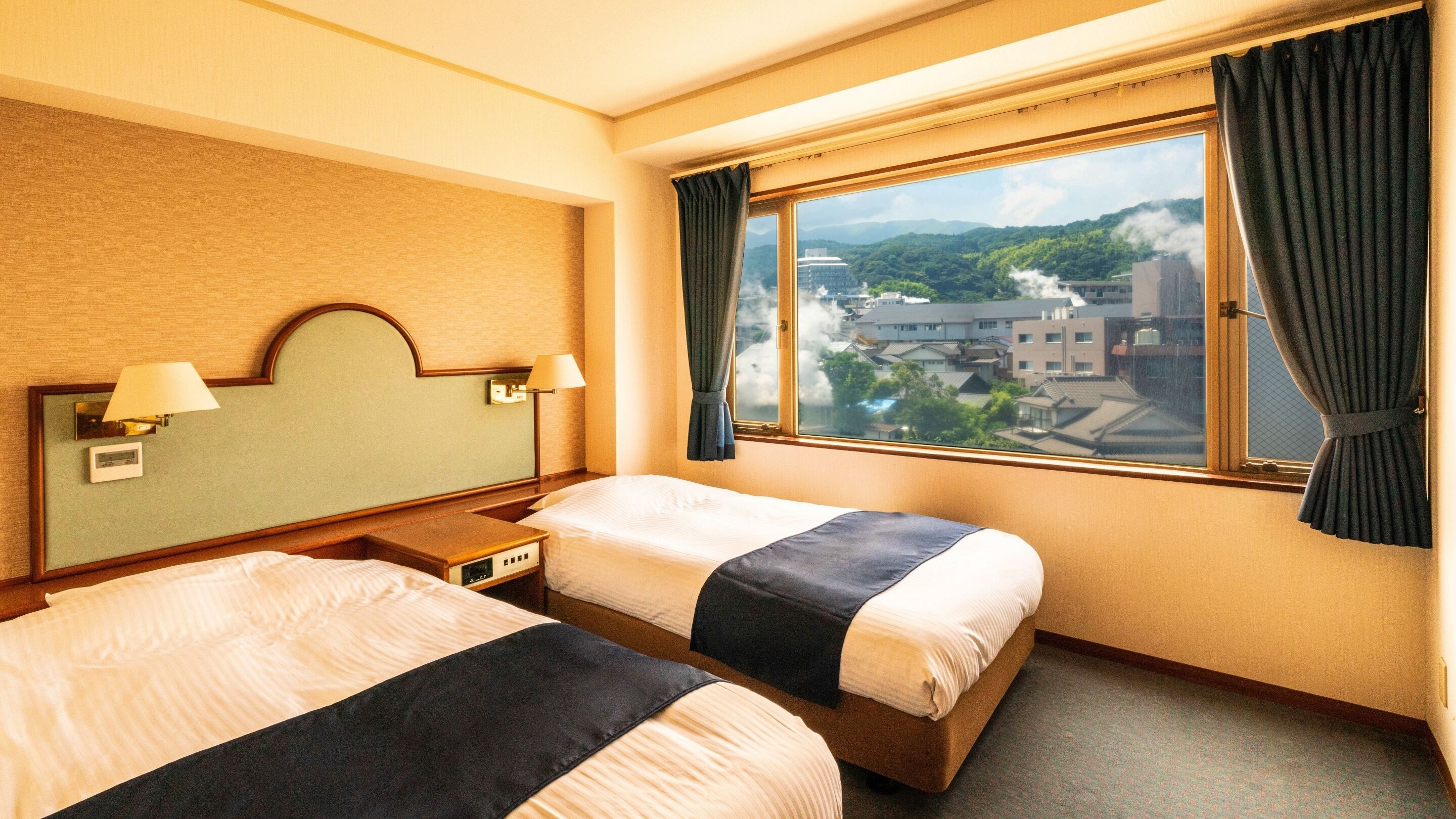 Quarto de hotel com duas camas, vista para a cidade e janela com cortinas.