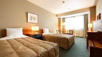 Quarto de hotel com duas camas, uma escrivaninha, uma cadeira, uma televisão e uma janela com cortinas.