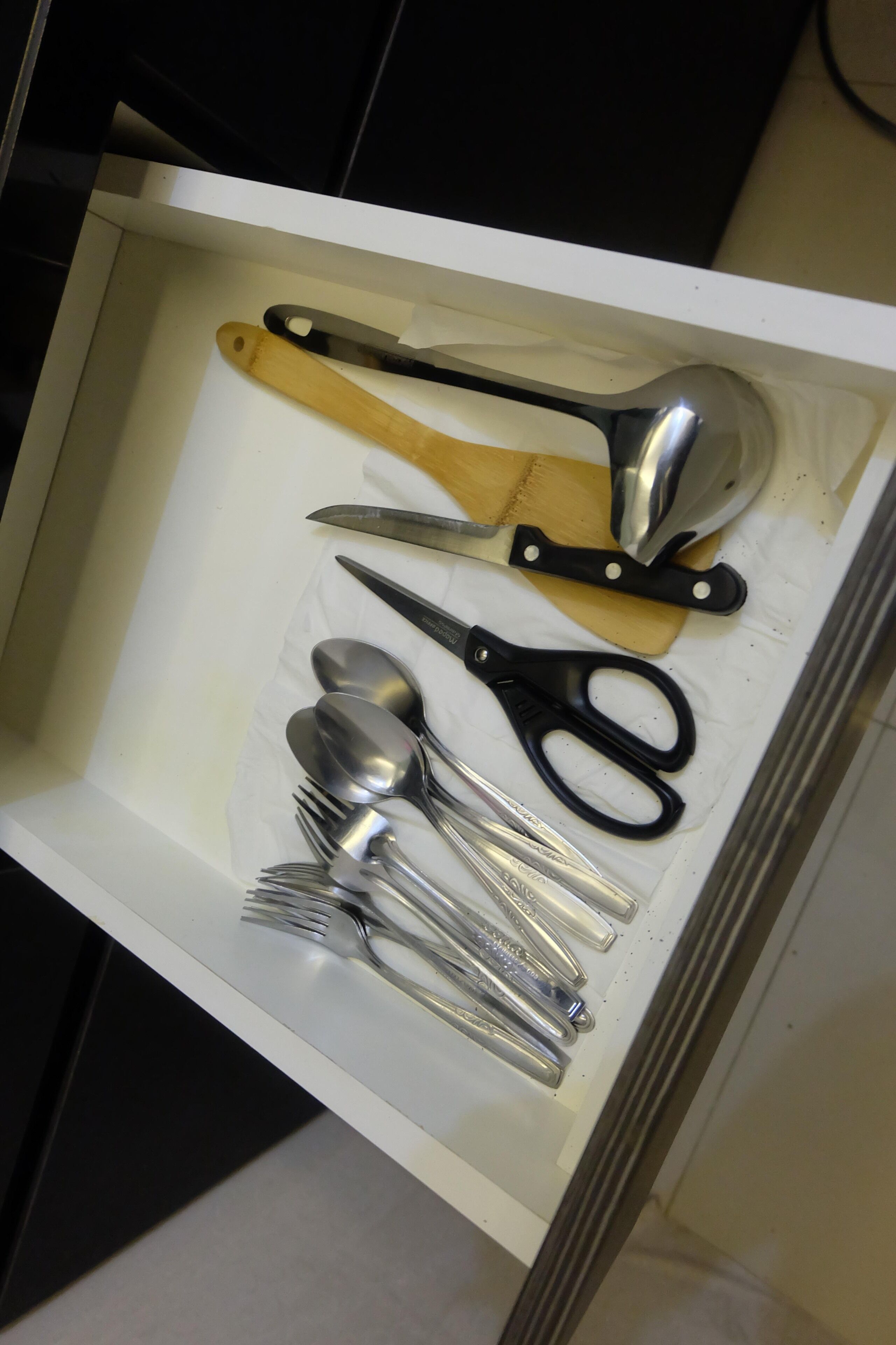 Uma gaveta com diversos utensílios de cozinha, incluindo faca, colher, garfo e tesoura.