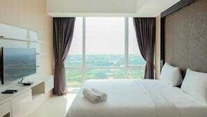 Quarto de hotel com uma cama grande, uma televisão de tela plana e vista para o campo através de uma janela ampla.