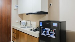 Uma cozinha compacta com armários brancos, uma geladeira preta, uma pia e um fogão.
