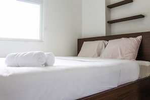 Uma cama bem arrumada com lençóis brancos, uma toalha enrolada, cabeceira de madeira e prateleiras embutidas acima da cama.