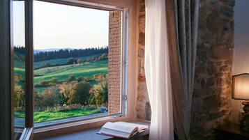 Quarto com janela para uma paisagem verde, um livro no parapeito e uma parede de pedra.