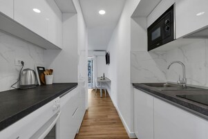 Cozinha moderna com armários brancos, bancada preta e piso de madeira.