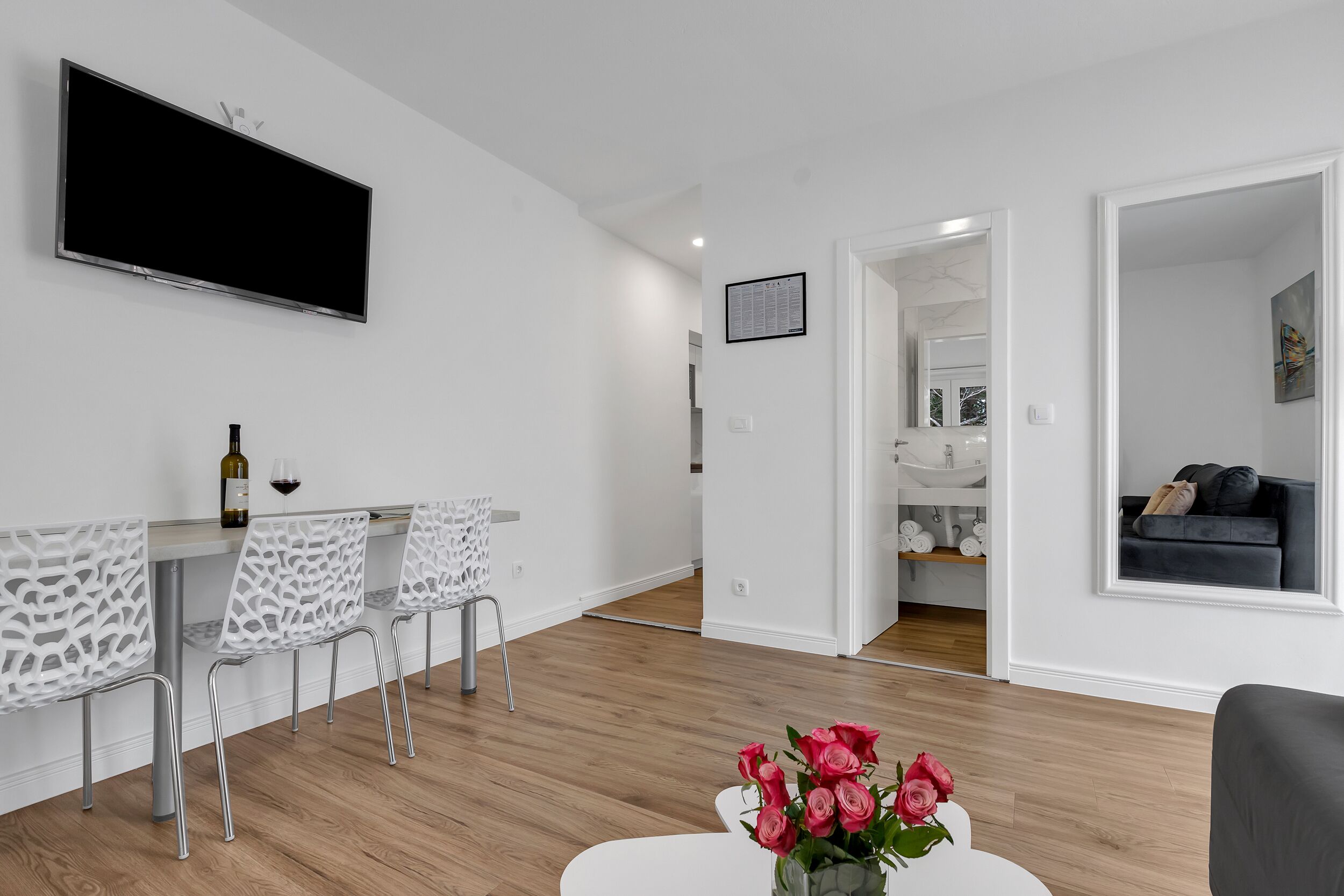 Uma sala de estar moderna com área de refeições, uma televisão na parede e um sofá em um quarto vizinho.