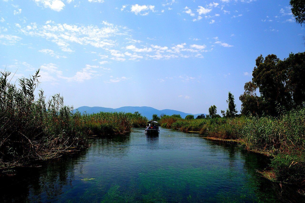 Um canal estreito com um barco, rodeado por vegetação densa e montanhas ao longe.