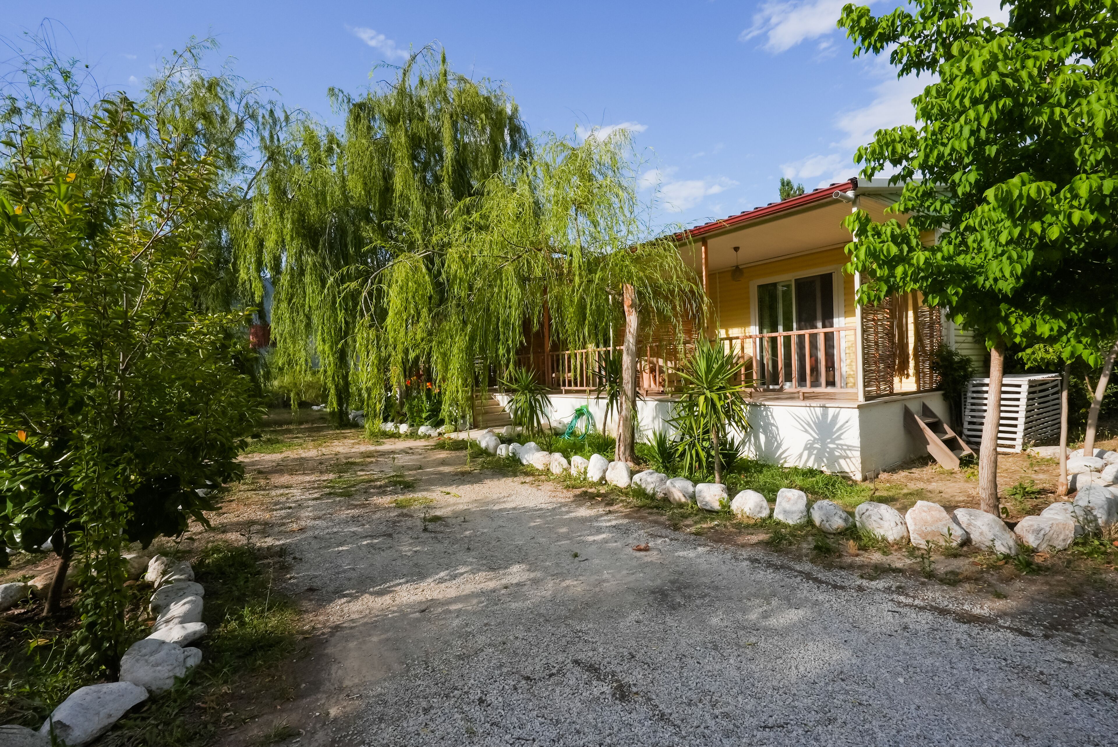 Uma casa com varanda, cercada por árvores e um caminho de cascalho.