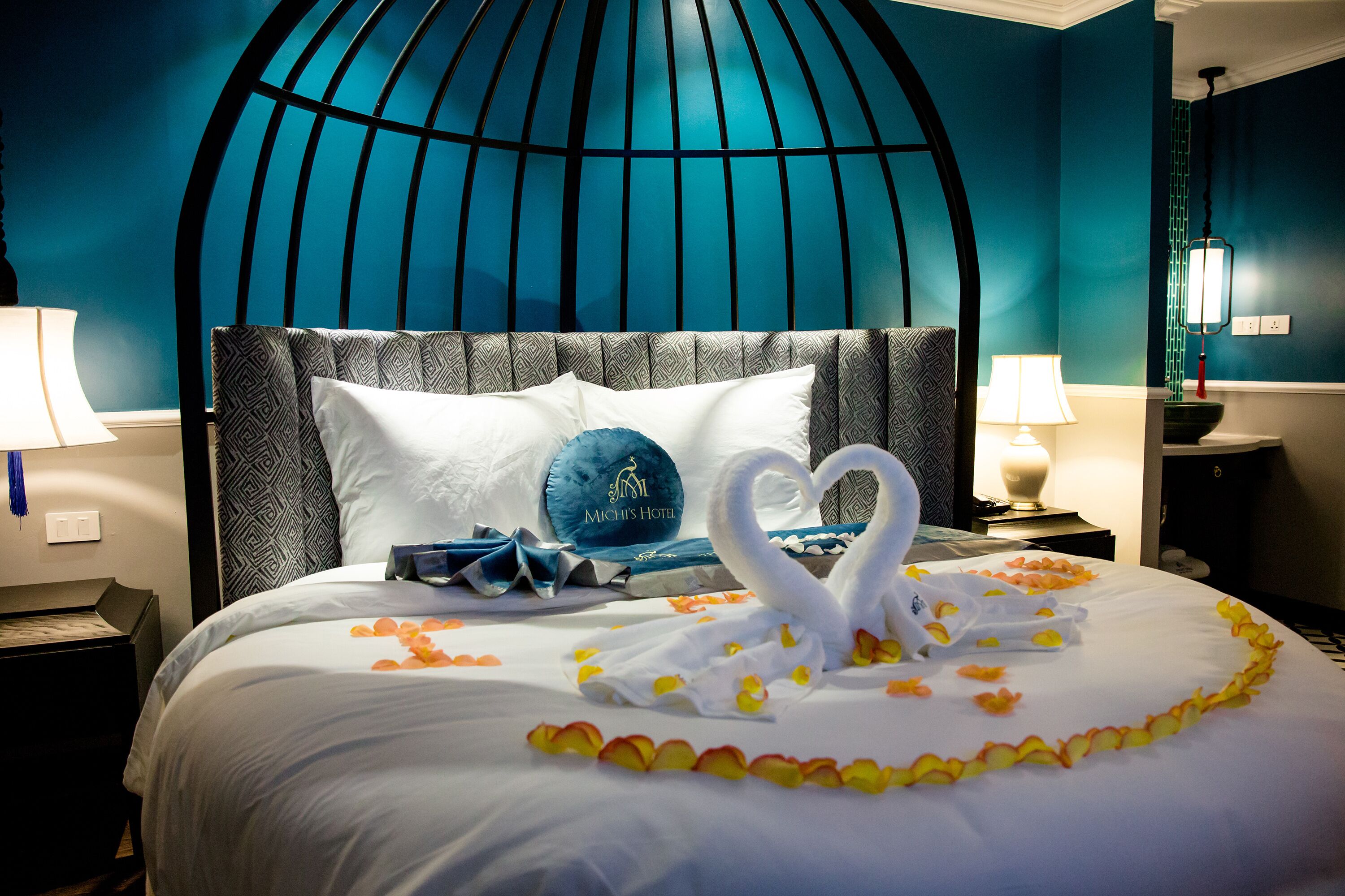 Quarto de hotel com uma cama grande, uma parede em tom azul e uma cabeceira de metal preta e diferenciada.