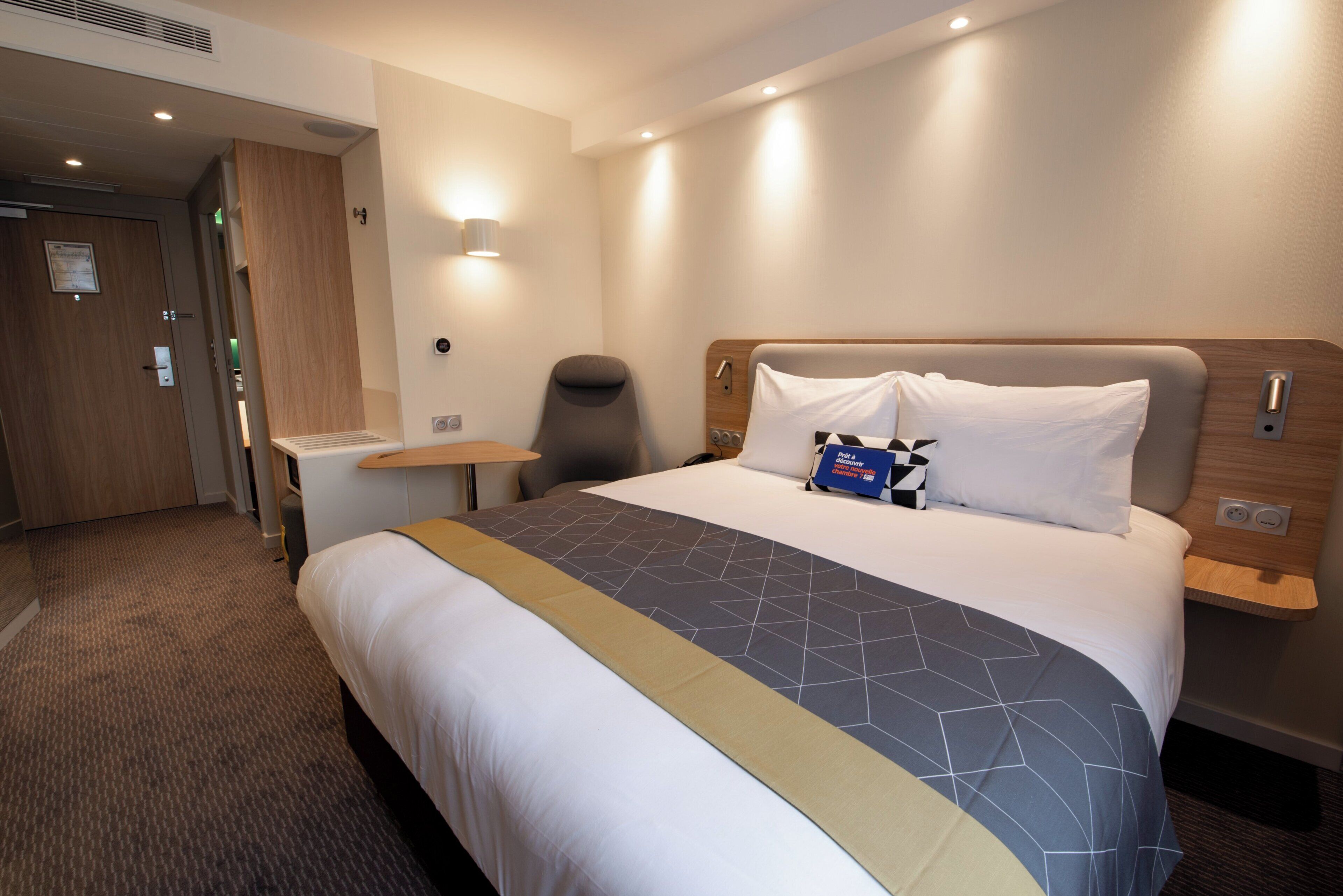 Quarto de hotel com cama, mesas de cabeceira, uma cadeira e escrivaninha.