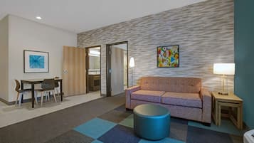 Um saguão de hotel com balcão de recepção, área de estar com sofá e apoio para os pés, carpete estampado e obras de arte nas paredes.
