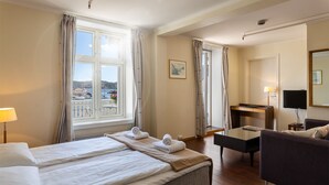 Quarto de hotel com duas camas, uma escrivaninha, um sofá e uma televisão.