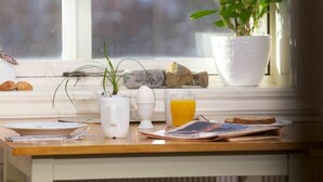 Uma mesa de café da manhã com uma planta, uma xícara, um copo de suco de laranja e um prato com fruta.