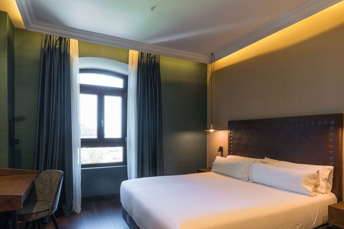 Quarto de hotel com cama, escrivaninha e janela com cortinas.