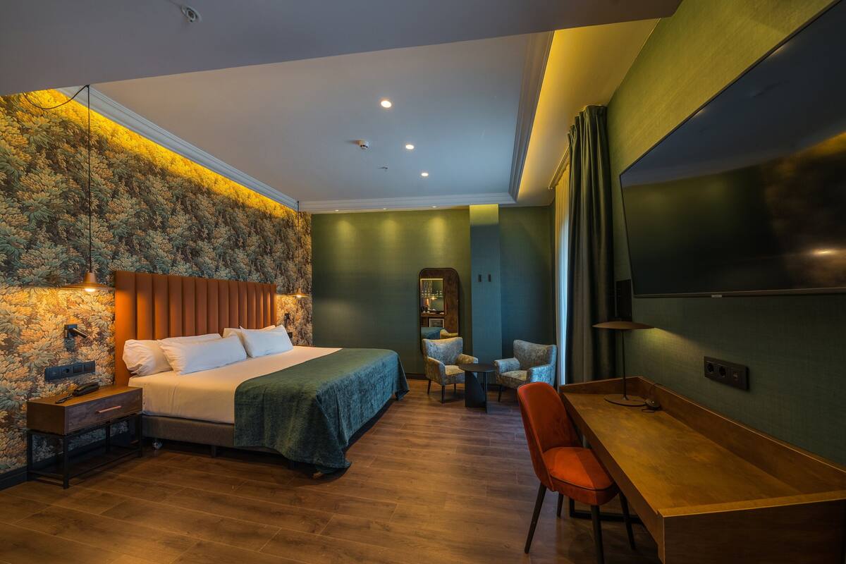 Quarto de hotel com uma cama, escrivaninha, cadeira, espelho e parede com textura.