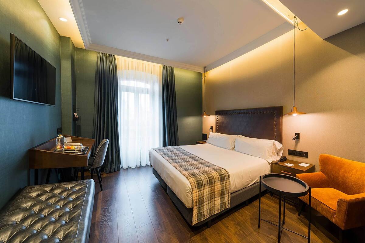 Quarto de hotel com cama, escrivaninha, cadeira, mesa pequena e sofá.