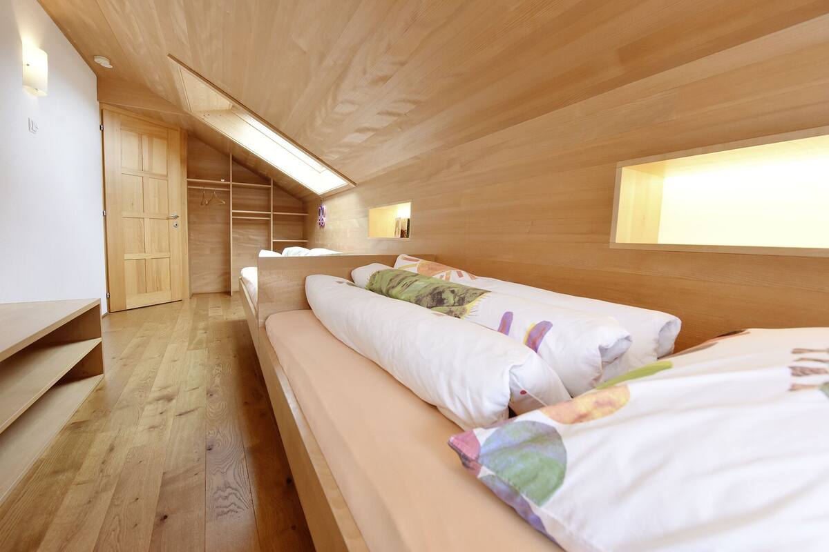 Quarto com duas camas, piso de madeira, claraboia e guarda-roupa.