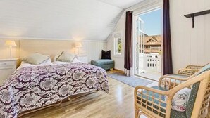 Quarto com uma cama grande, mesa de cabeceira, cadeira e vista para o exterior.