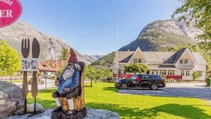 Uma pousada de montanha com uma estátua de pedra de uma pessoa num chapéu vermelho, uma sala de jantar e vista para as montanhas.