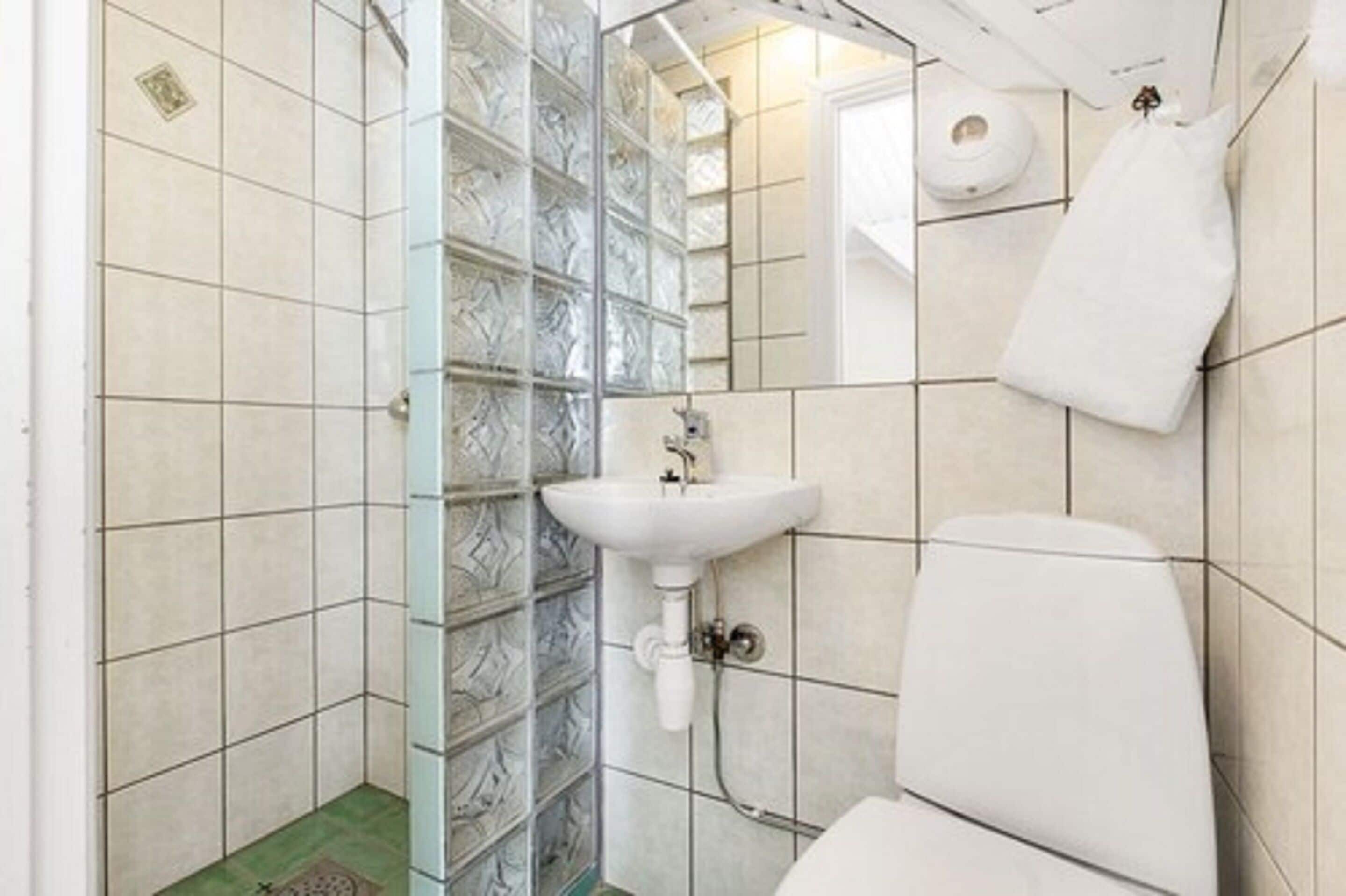 Casa de banho com soalho em mosaico, lavatório, sanita e área de duche com portas de vidro.