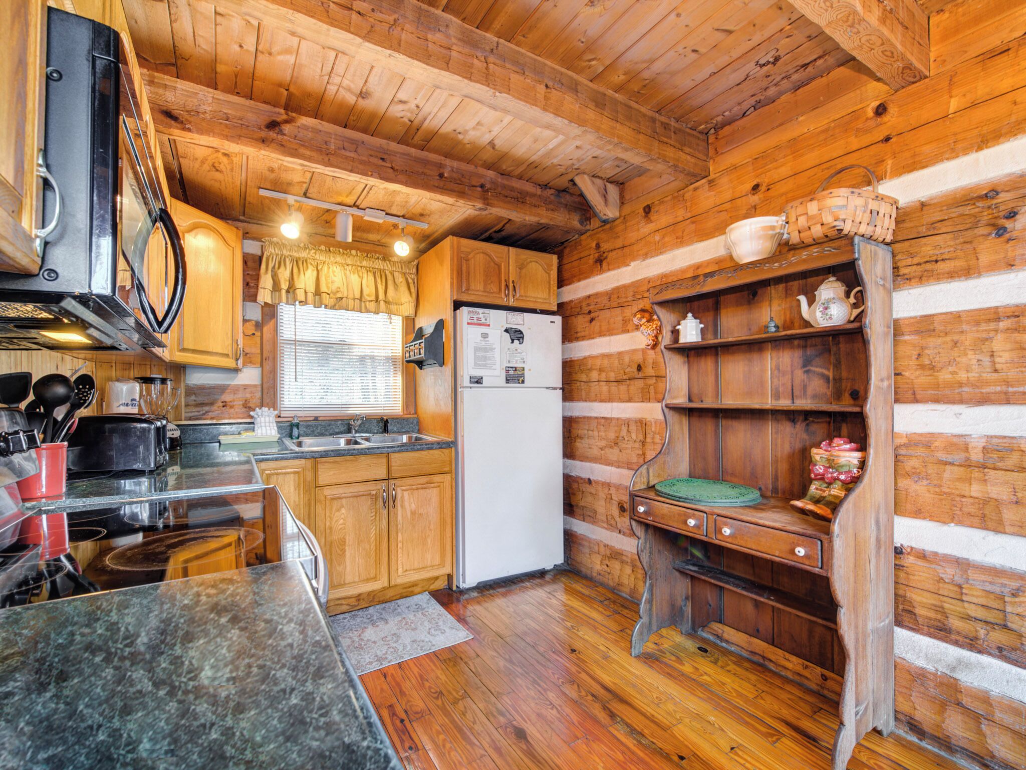 Interior de uma cabana de madeira com cozinha, incluindo armários de madeira, uma geladeira e bancada com diversos utensílios.