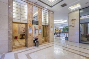 Um saguão de hotel com uma recepção, um quiosque de informações digitais e um vaso de plantas.