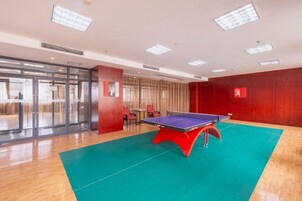 Um quarto com mesa de pingue-pongue, carpete verde e parede vermelha.