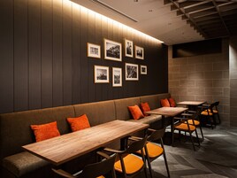 Interior de restaurante moderno com um longo banco de madeira, almofadas laranja e quadros nas paredes.