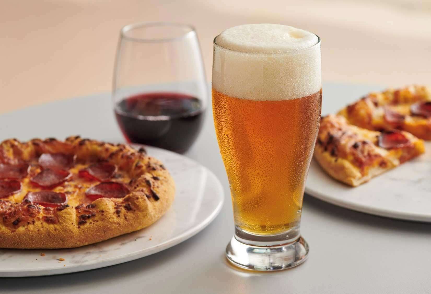 Pizza com pepperoni e um copo de cerveja sobre uma mesa.