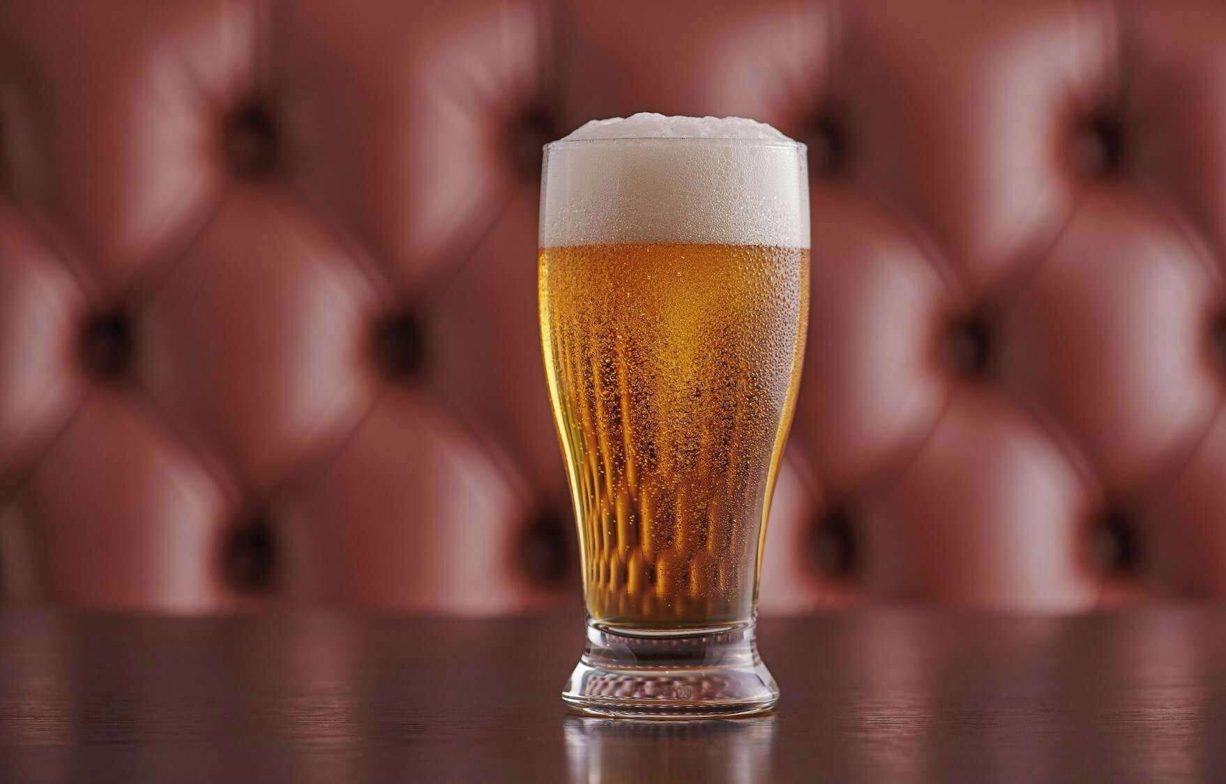 Um copo alto de cerveja sobre uma mesa de madeira, com um fundo de couro vermelho.