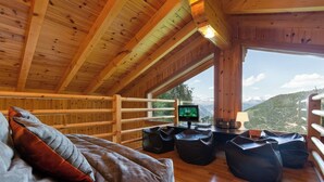 Quarto de cabana de madeira com uma cama, uma escrivaninha com computador e vista para montanhas.