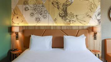 Quarto de hotel com cama, duas almofadas, cabeceira de madeira, parede com padrões florais e abstratos, e duas luminárias de cabeceira.
