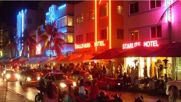 Rua movimentada com dois hotéis, Boulevard Hotel e Starlite Hotel, apresentando letreiros de neon e mesas ao ar livre.