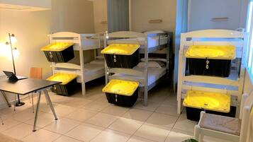 Quarto em dormitório com beliches e caixas organizadoras, uma escrivaninha com um laptop e uma cadeira.