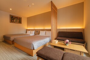 Quarto de hotel com duas camas, um sofá, uma mesinha com um vaso de flores e um quadro na parede.