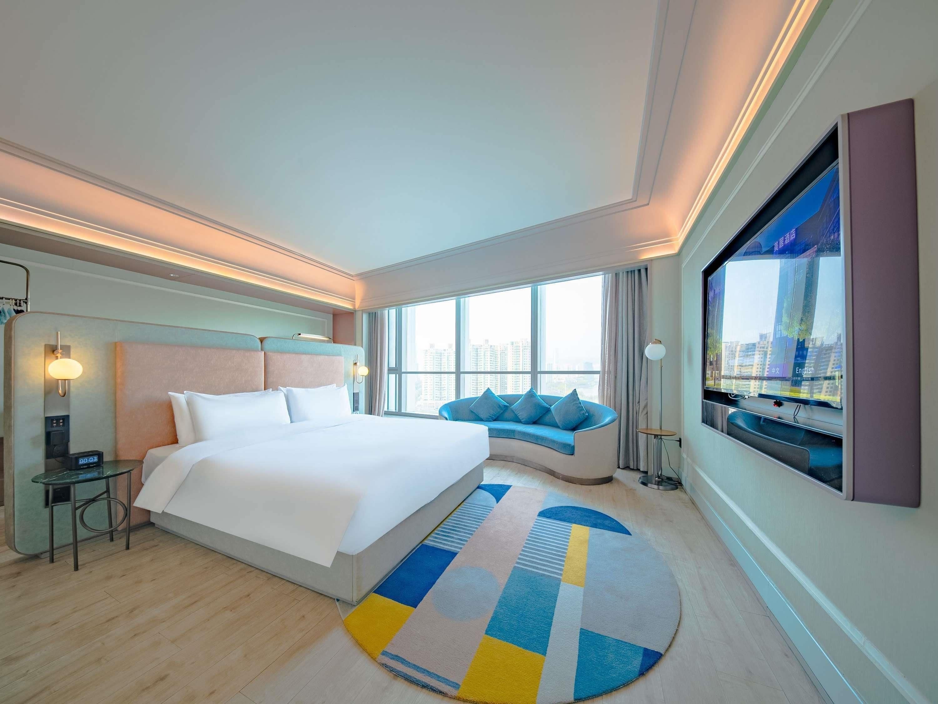 Quarto de hotel com uma cama grande, um sofá, uma televisão e vista para a cidade.