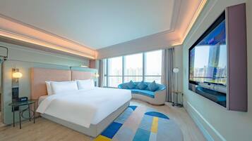 Quarto de hotel com uma cama grande, um sofá, uma televisão e vista para a cidade.
