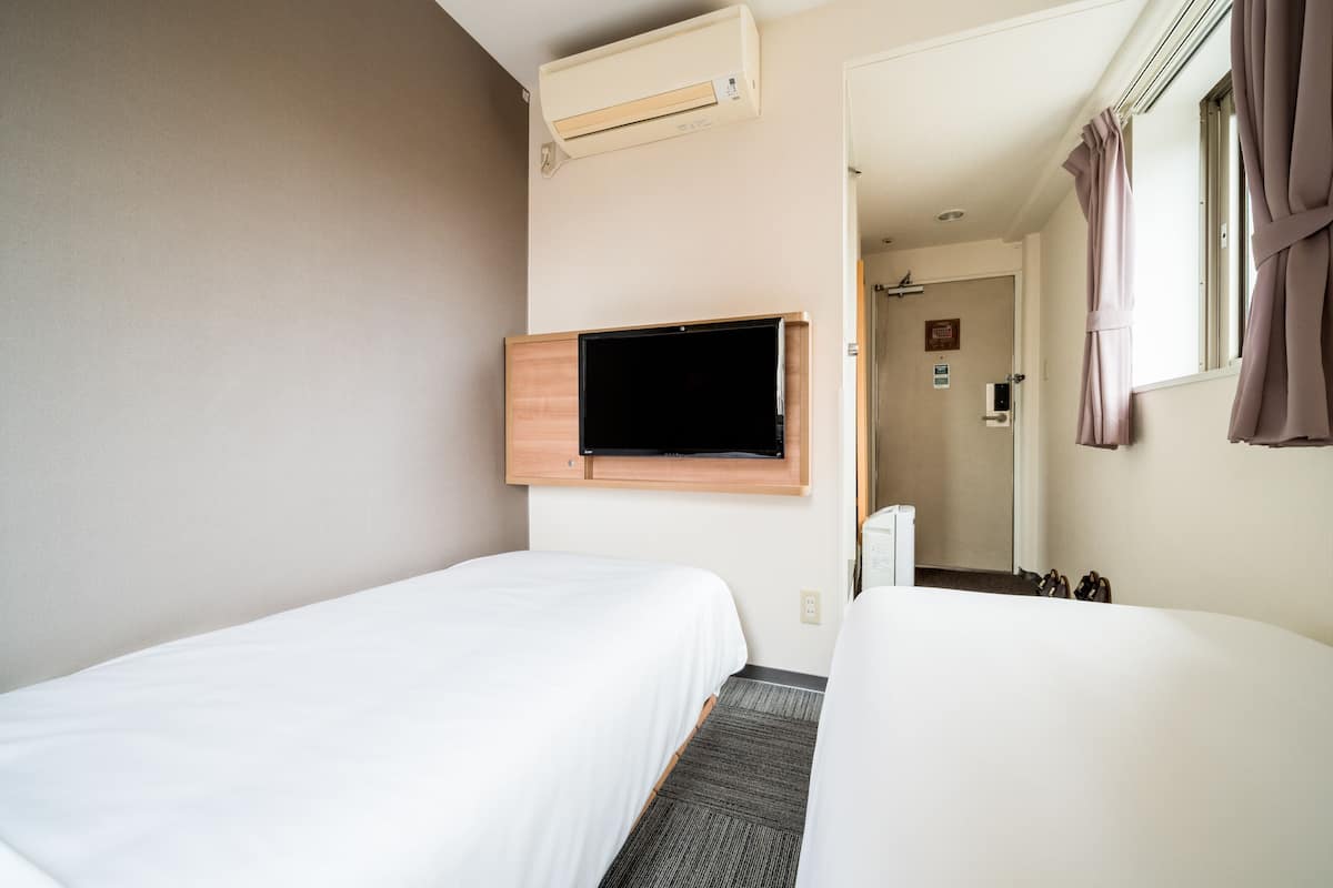 Quarto de hotel com duas camas, uma TV de tela plana na parede, ar-condicionado e uma janela com cortinas.